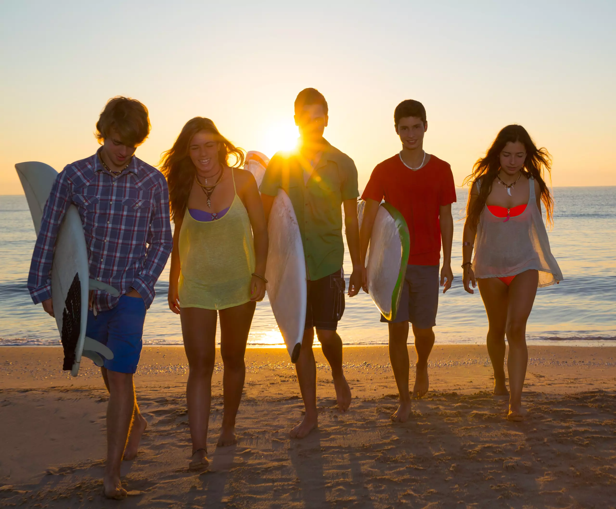 گروه دختران و پسران موج سوار در حال قدم زدن در ساحل