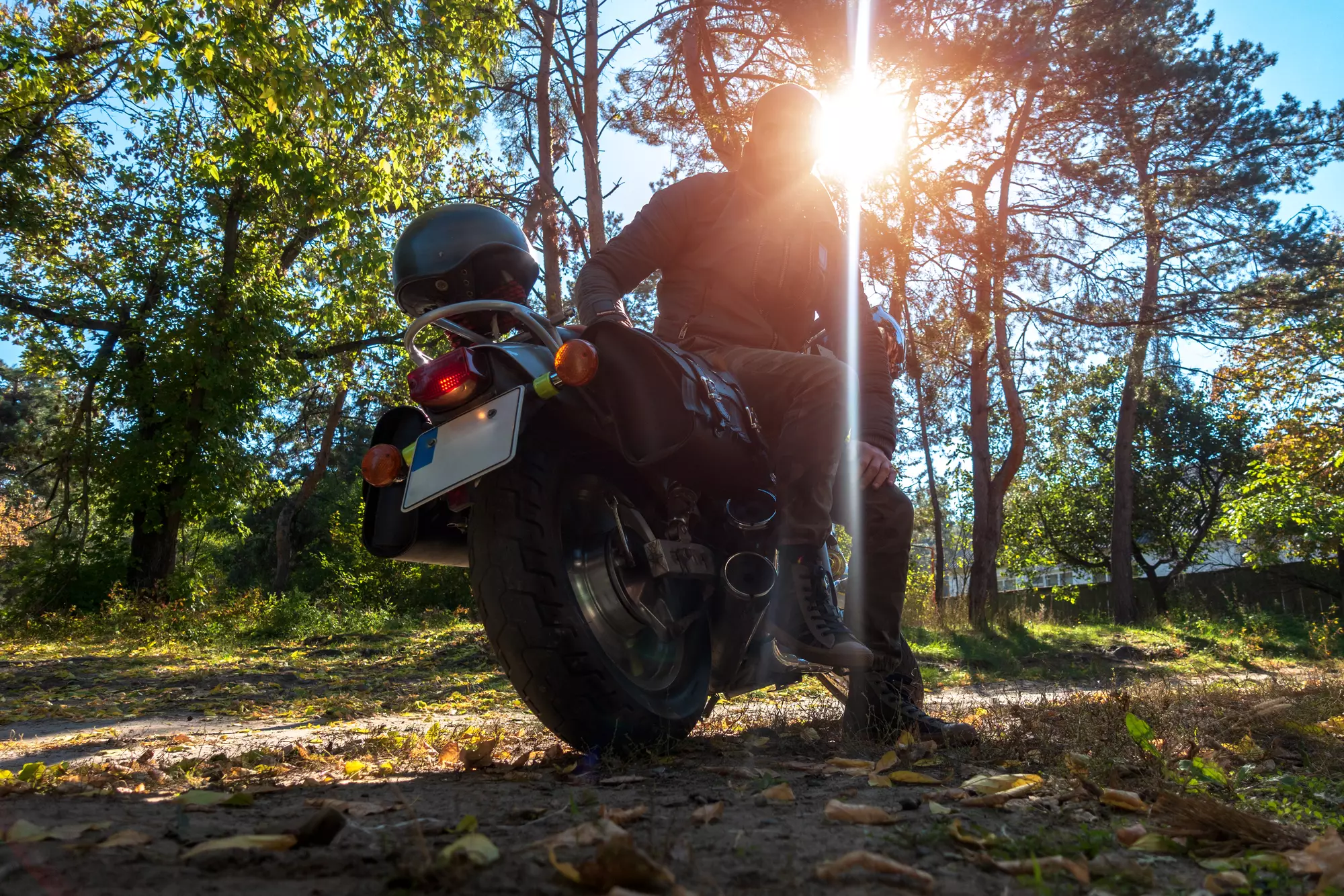 जंगलाच्या पार्श्वभूमीवर एक माणूस रेट्रो मोटरसायकलवर बसला आहे.